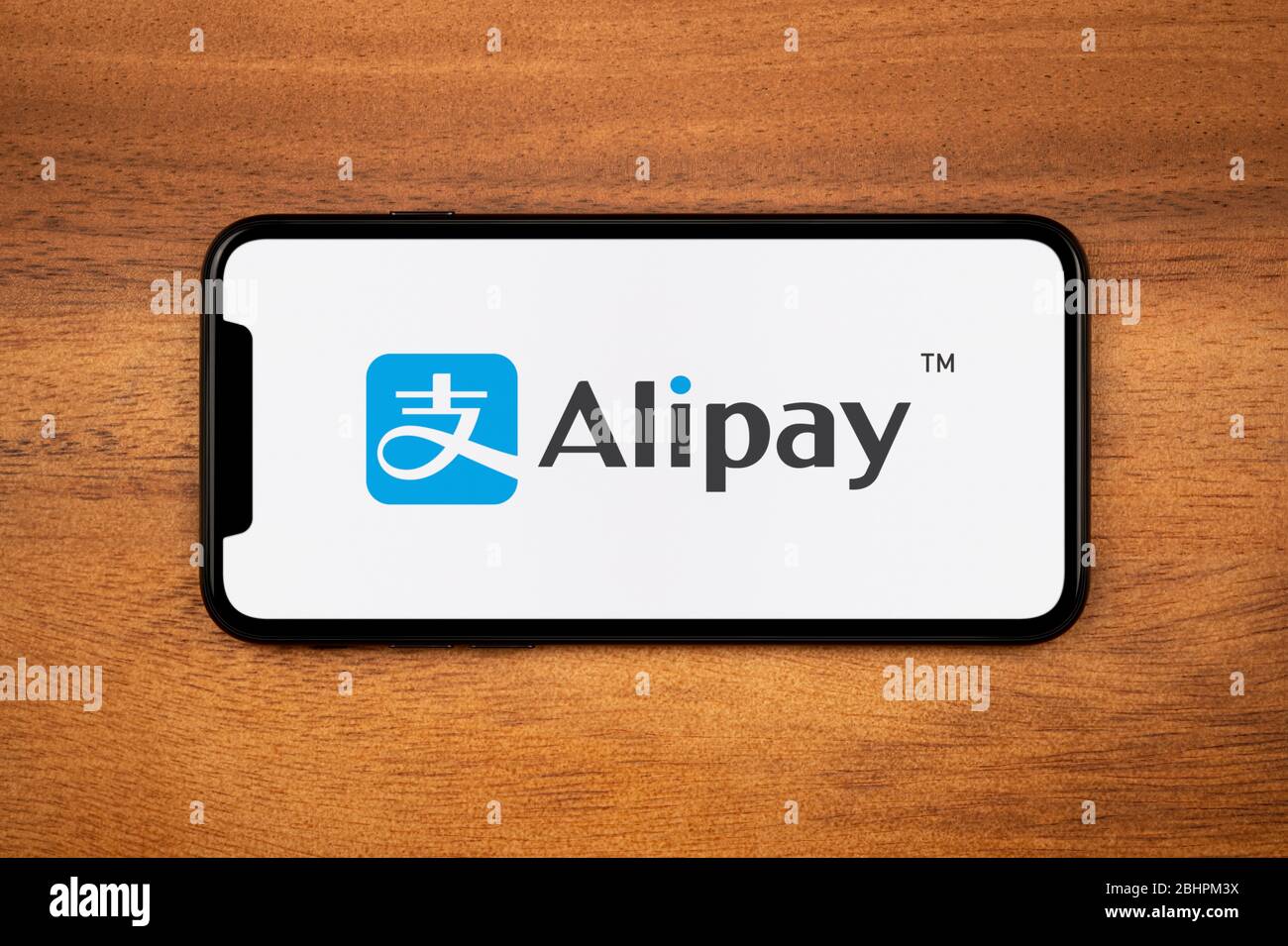 A smartphone showing the Alipay logo rests on a plain wooden table ...