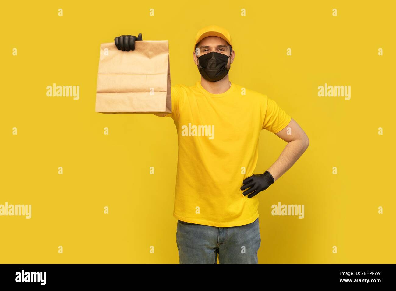 Delivery man employee in yellow cap t-shirt uniform mask glove hold ...