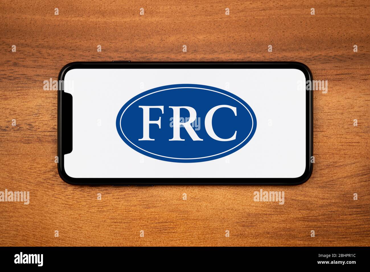 A smartphone showing the FRC logo rests on a plain wooden table ...