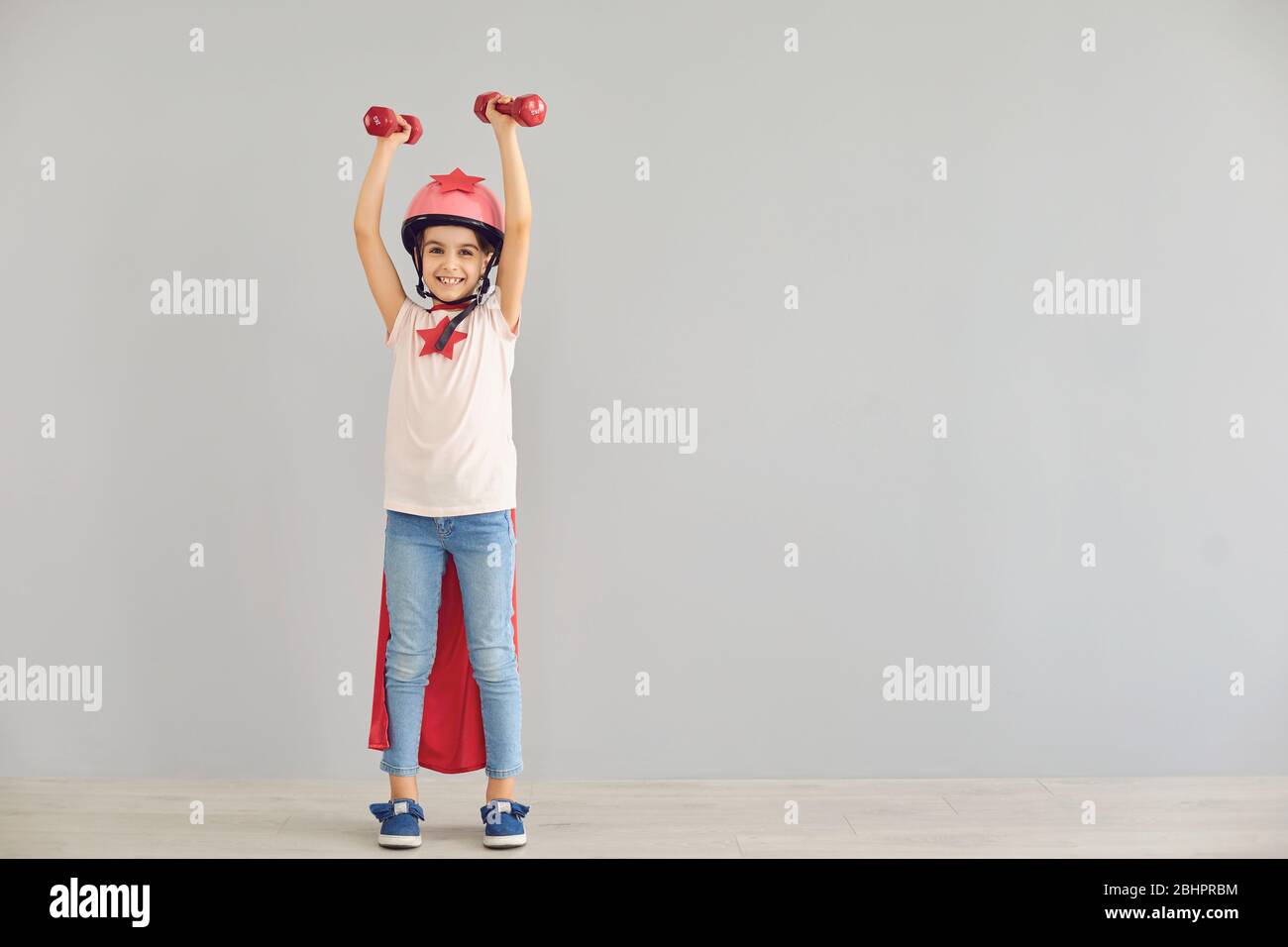 A child in a costume of a super hero raised his hands up with dumbbells ...
