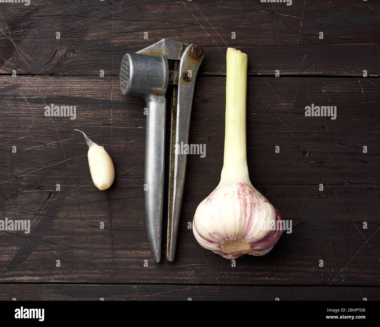 old metal garlic press and fresh young white garlic on a brown wooden ...