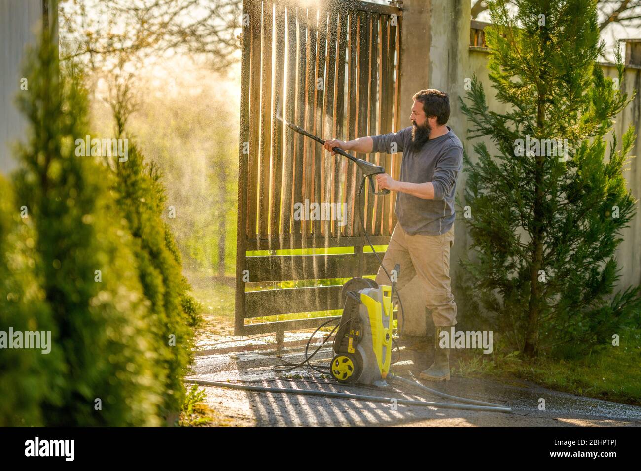 Mid adult man cleaning a wooden gate with a power washer. High water ...