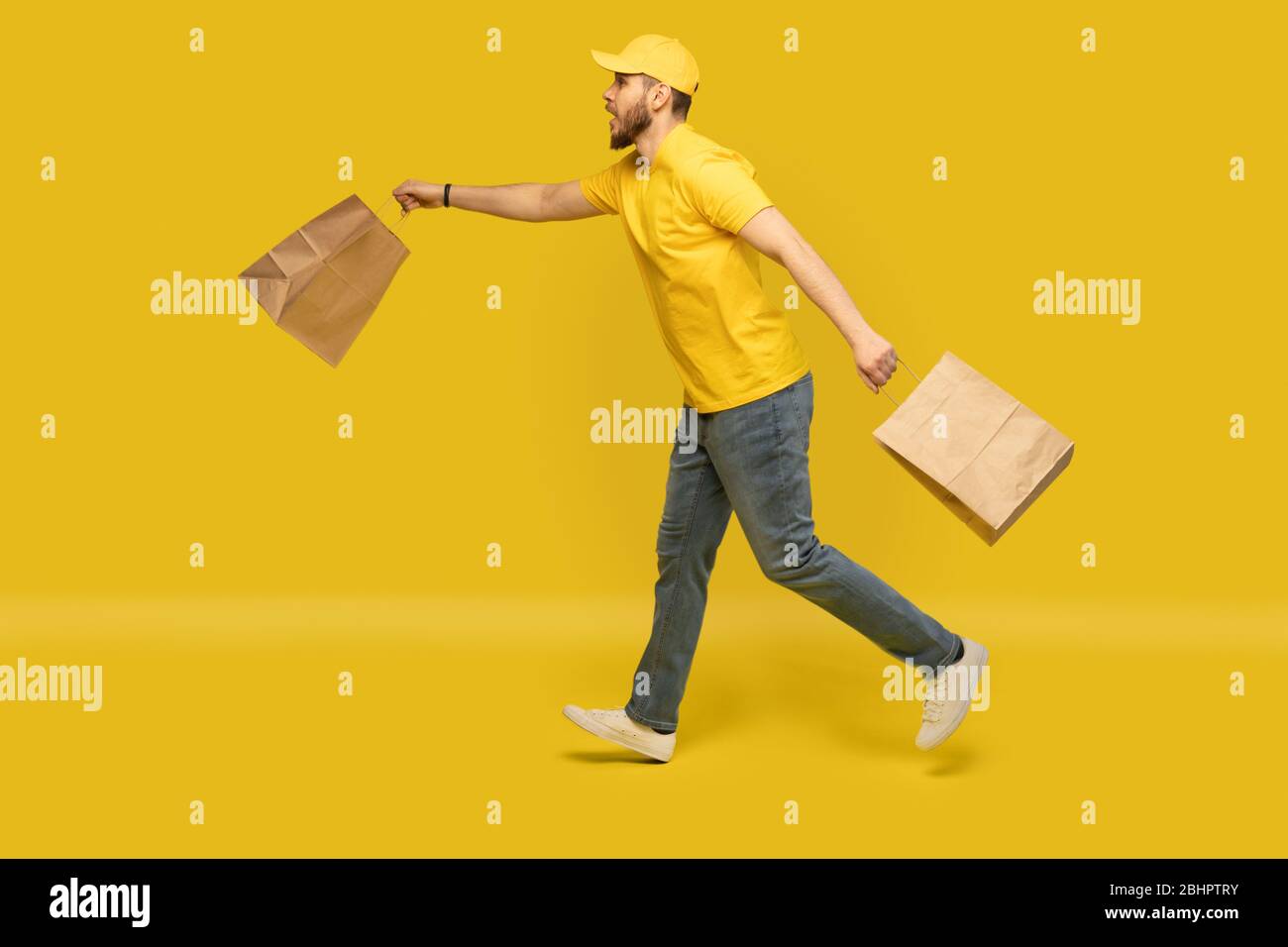 Portrait of young delivery man in yellow uniform running with paper ...
