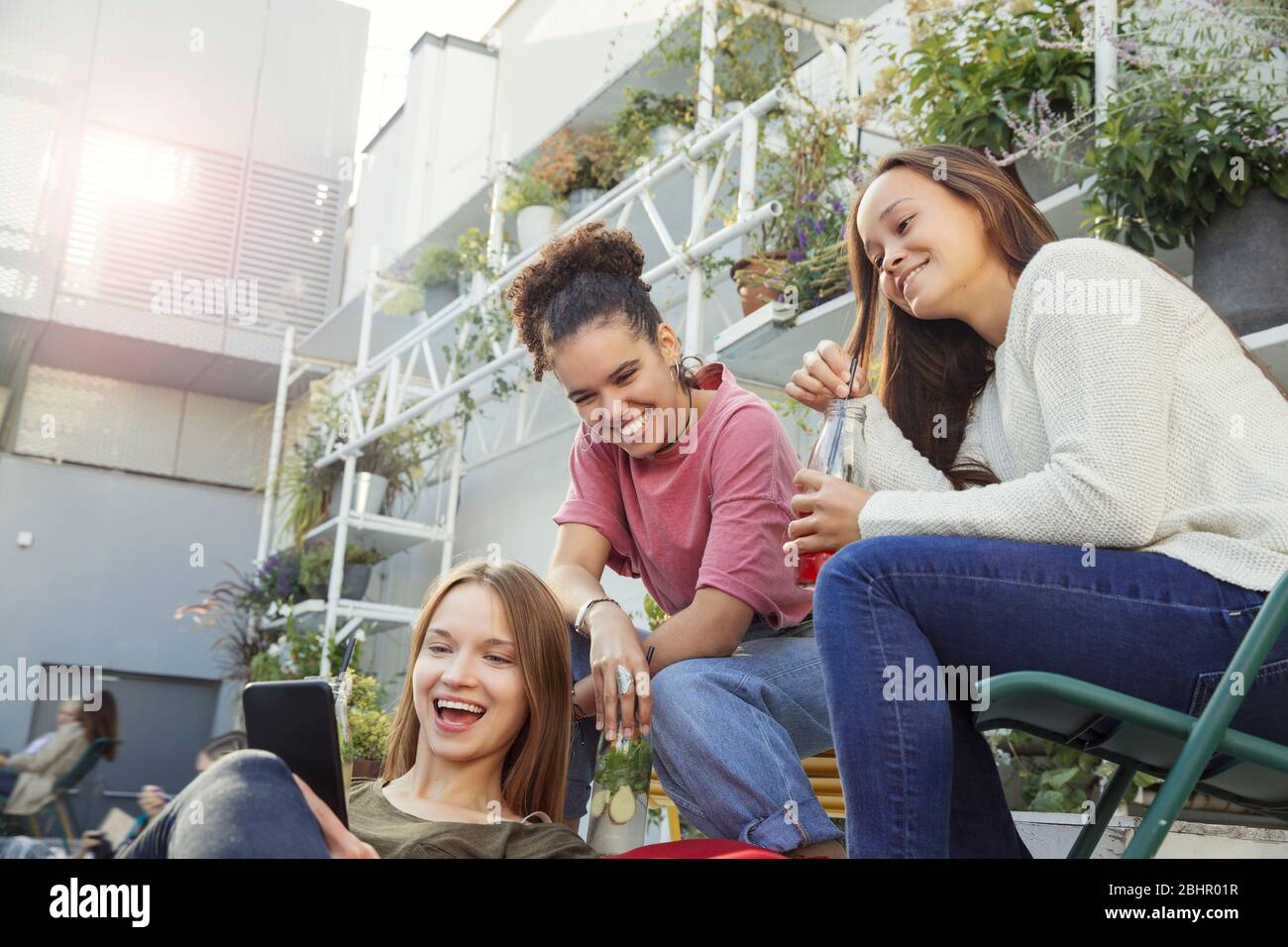 Three women sitting together and laughing, looking at a mobile phone ...