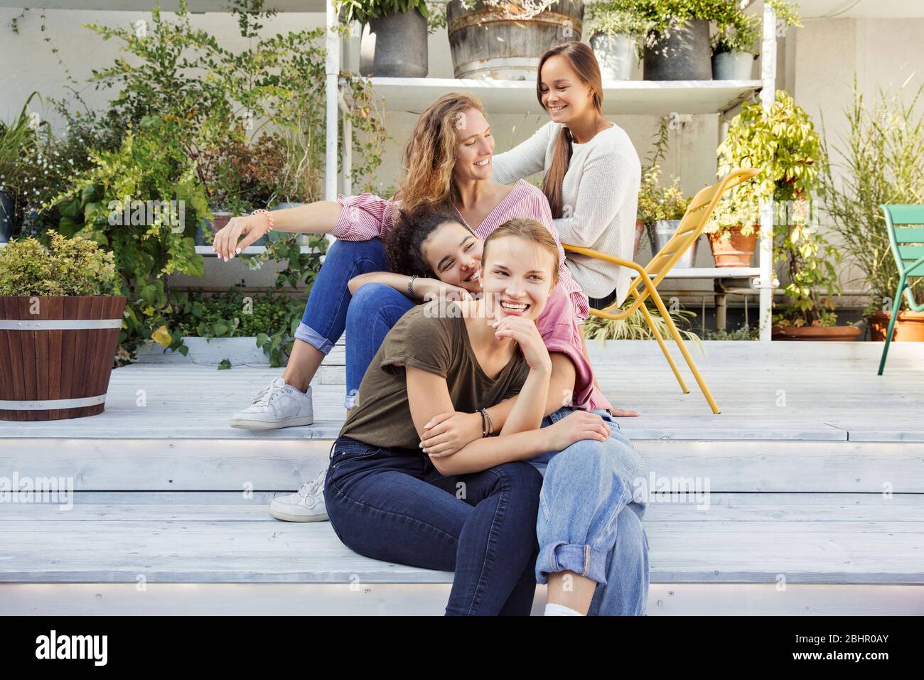 Four smiling women sitting in a courtyard with plants in the background ...