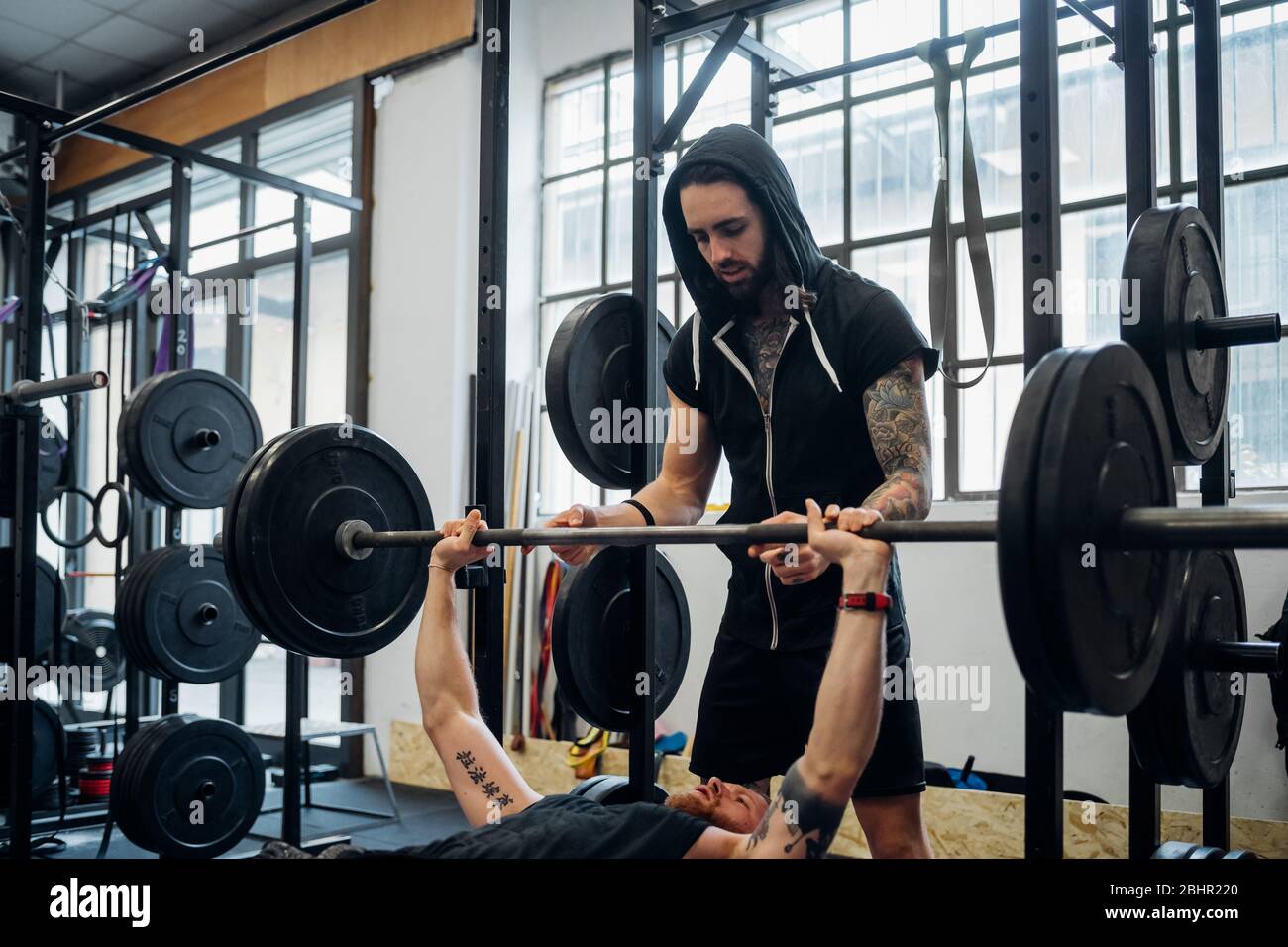 One man bench pressing a weight with another standing behind with hands ...