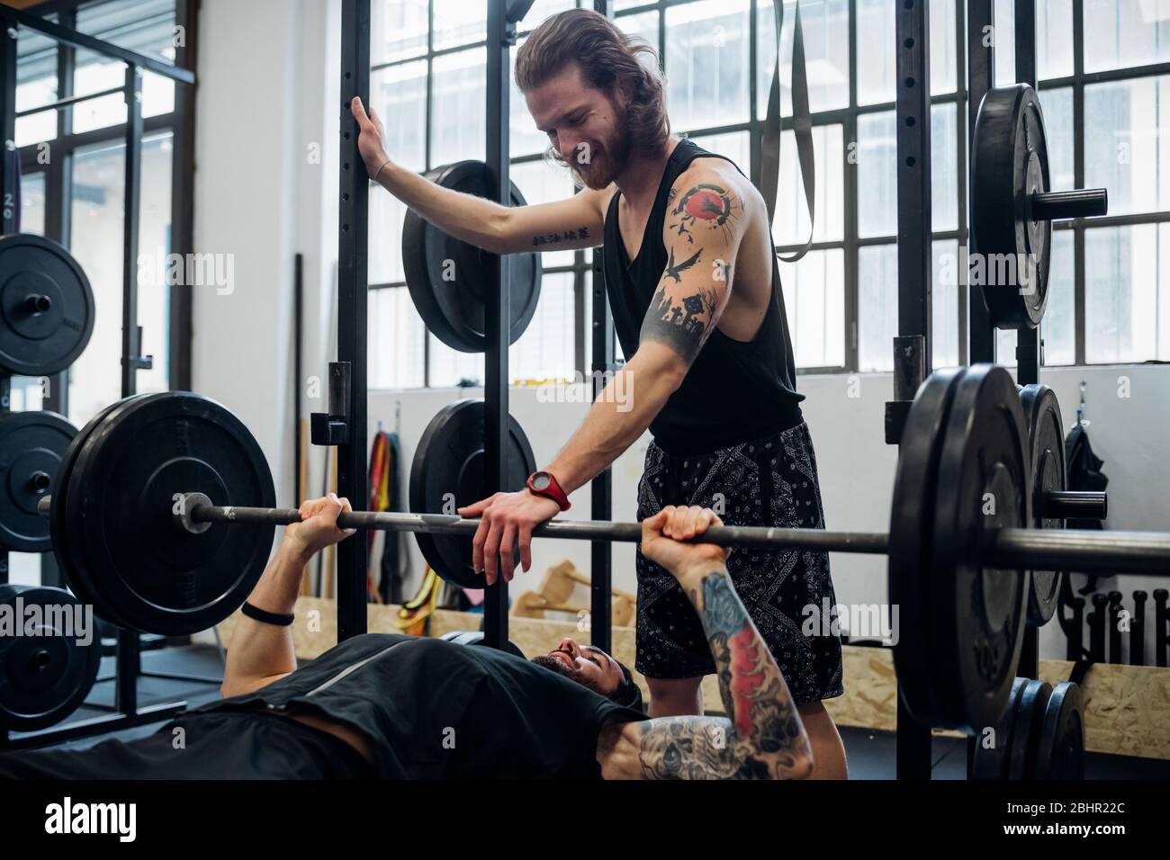 Man lying on a weight bench about to bench press with another man ...