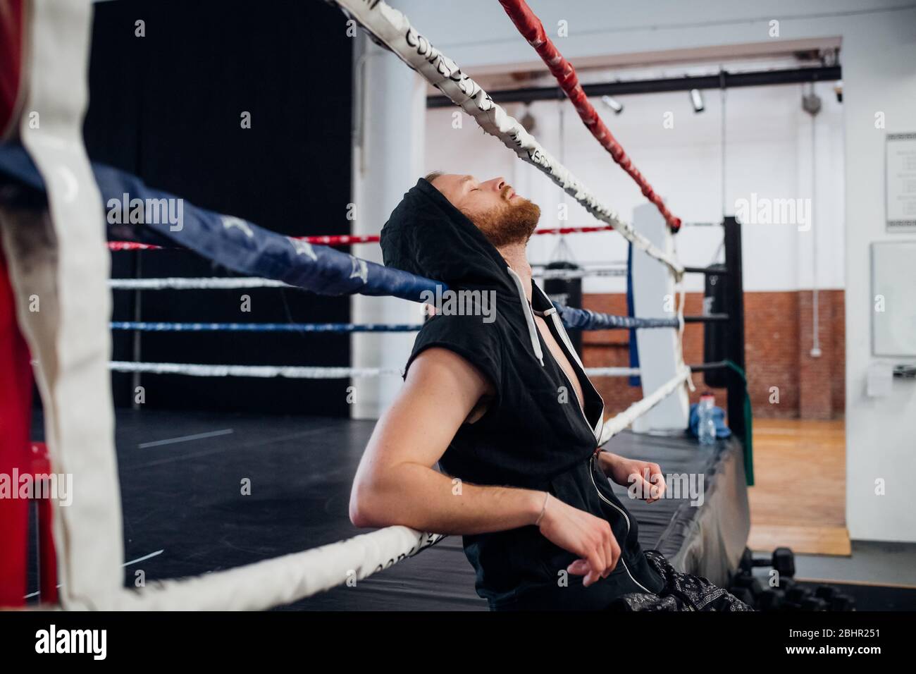 A man leaning against a boxing ring, head resting on a rope looking up ...