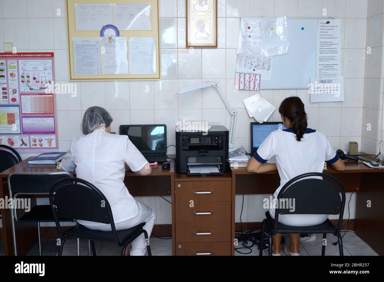 Two nurses sitting in the nurse station and writing in a paper, at the ...