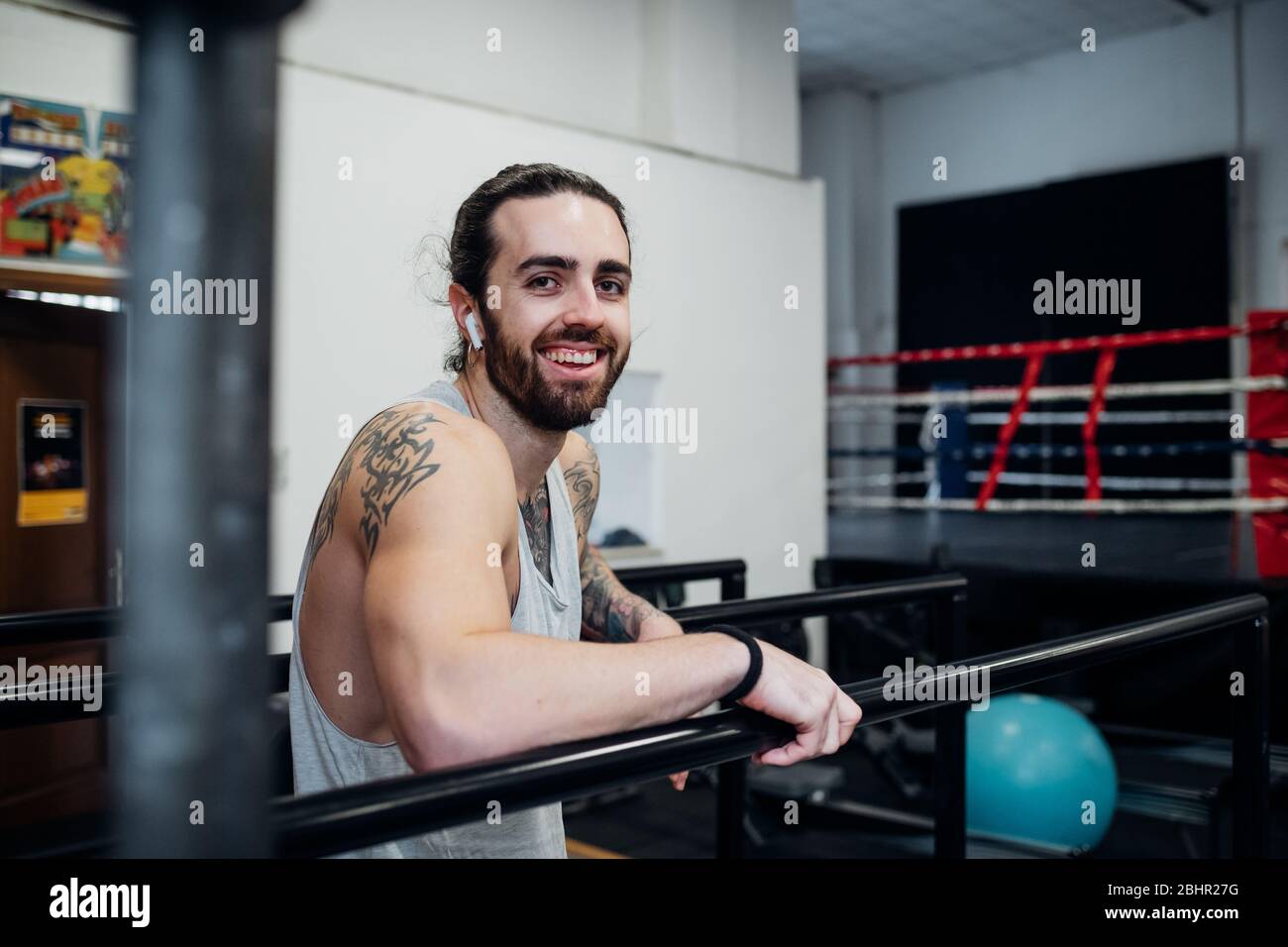 A smiling man standing next to a metal bar in a gymnasium with an ...