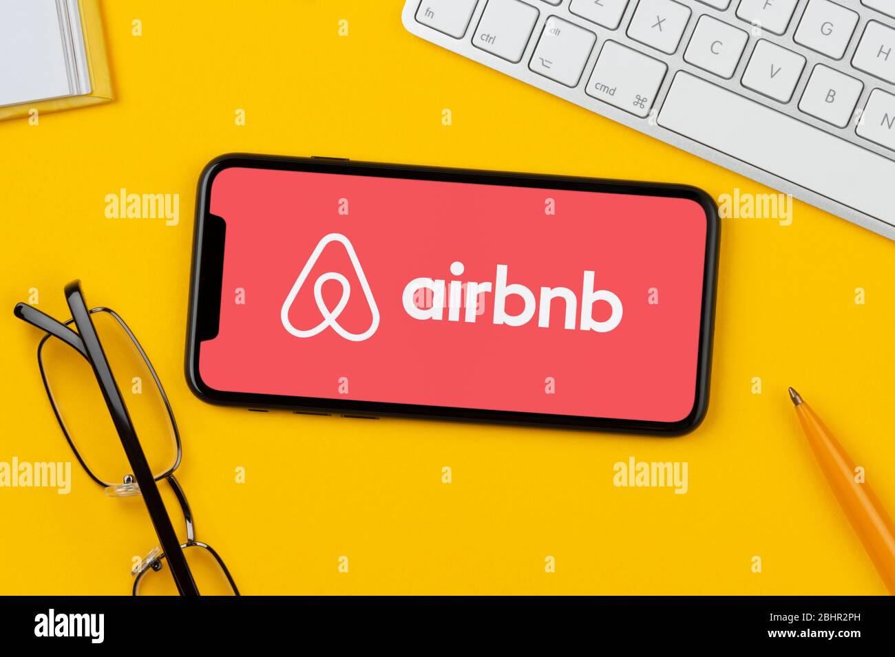 A smartphone showing the Airbnb logo rests on a yellow background along ...