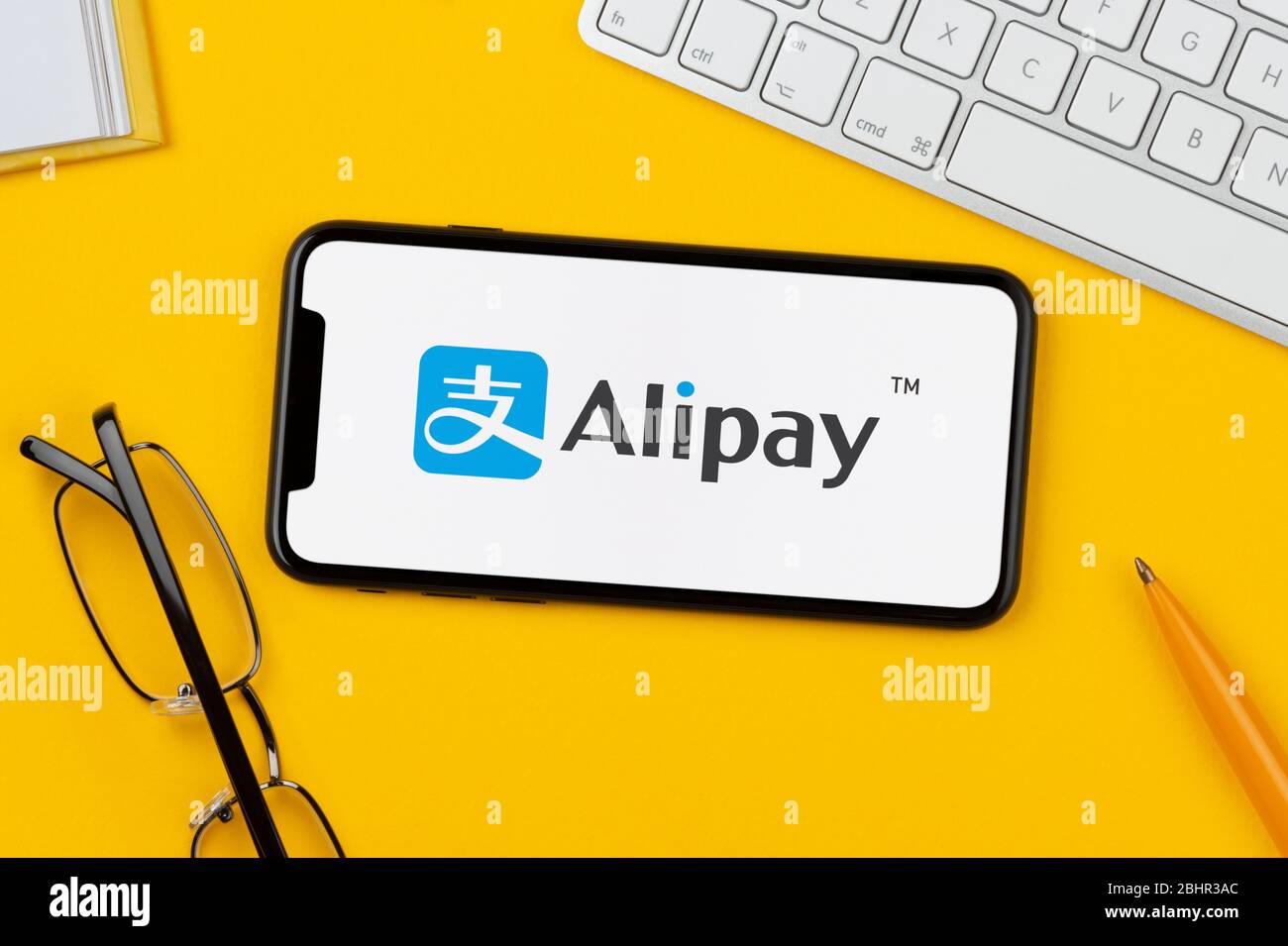 A smartphone showing the Alipay logo rests on a yellow background along ...