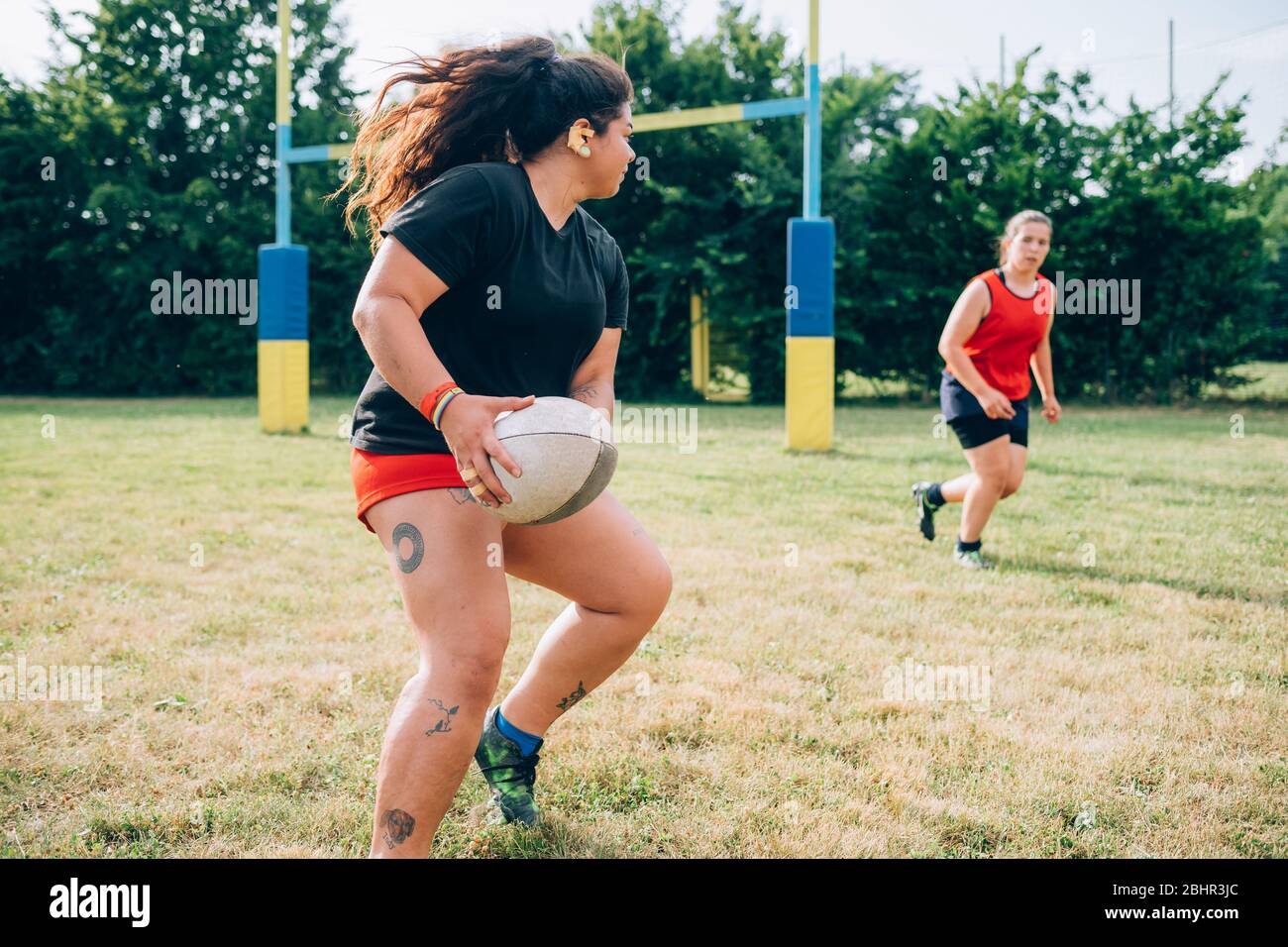 Two women running on a pitch one about to pass a rugby ball to the ...