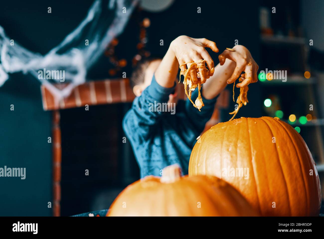 A child pulling their hands out of a pumpkin covered in seeds and ...