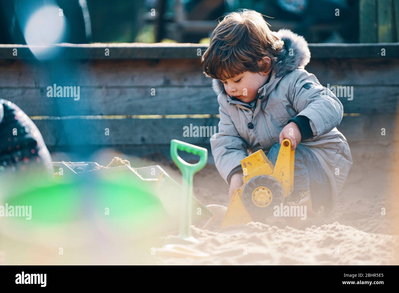 A child in a sandpit with a toy digger and spade Stock Photo - Alamy