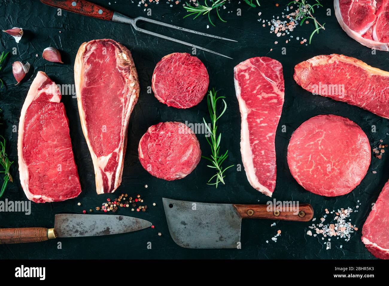 Cuts of meat variety, shot from above on a black background with salt ...