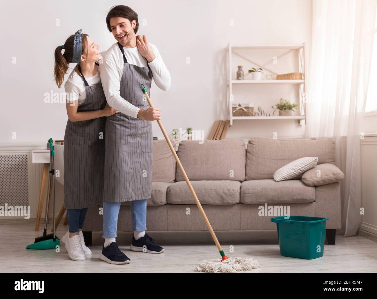 Joyful young couple doing spring-cleaning together, mopping floor and ...