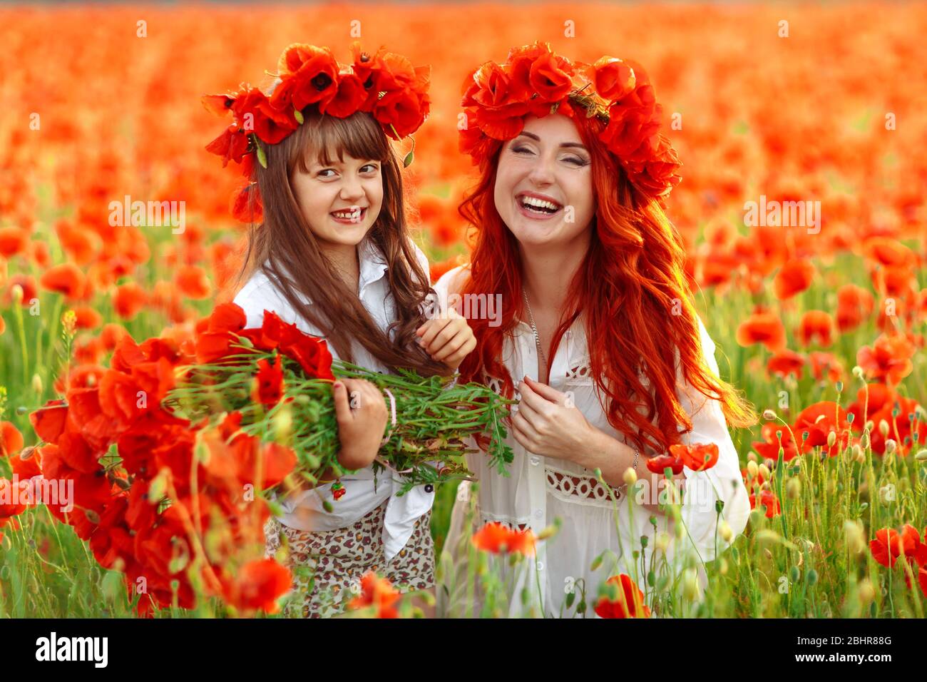 Little girl with redhead mother in white dresses and wreathes poses ...