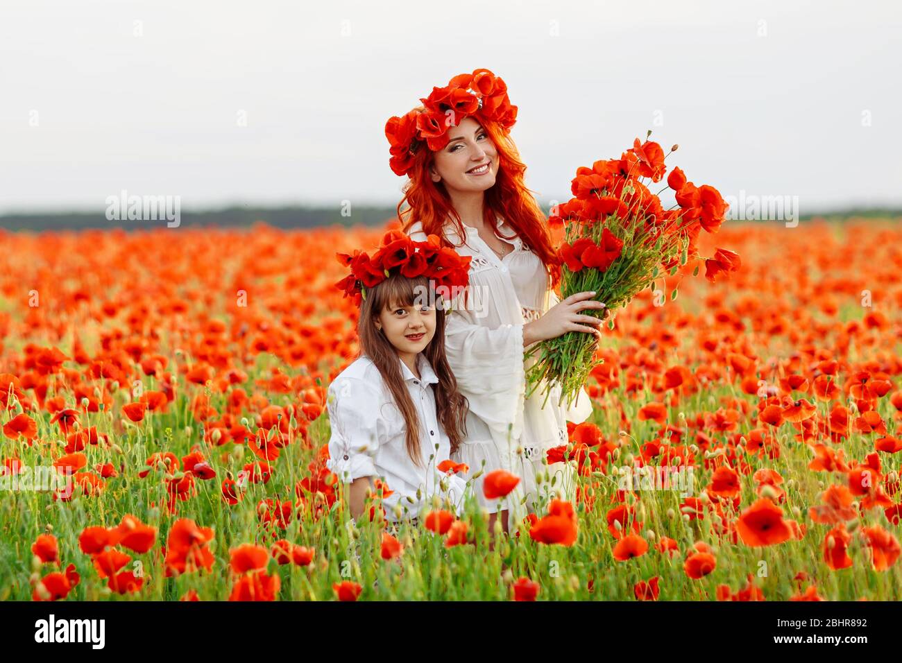 Little girl with redhead mother in white dresses and wreathes poses ...