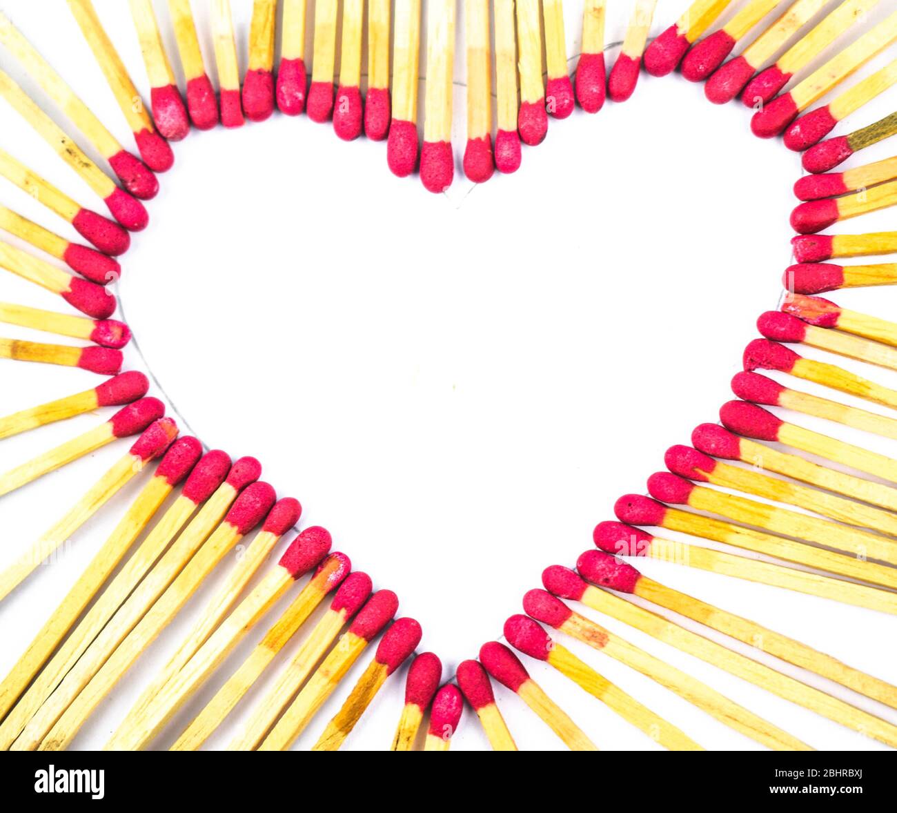 Heart made with red colored match sticks in front of a white isolated ...