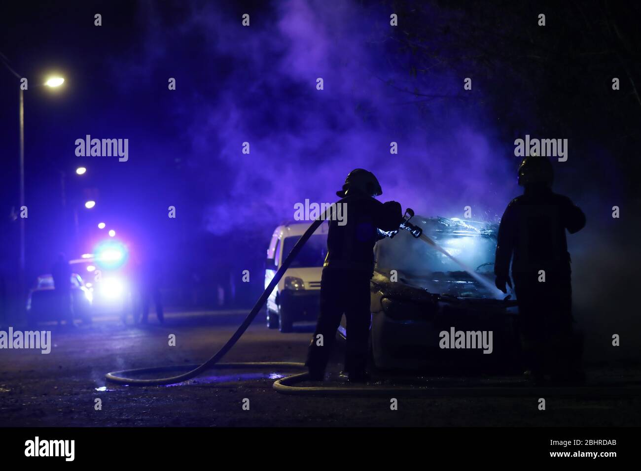 firefighters fighting against the fire in the midnight. Police car in a ...
