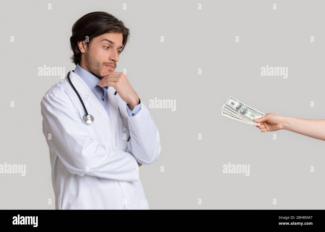Doubtful young doctor looking at money bribe offered by female patient ...