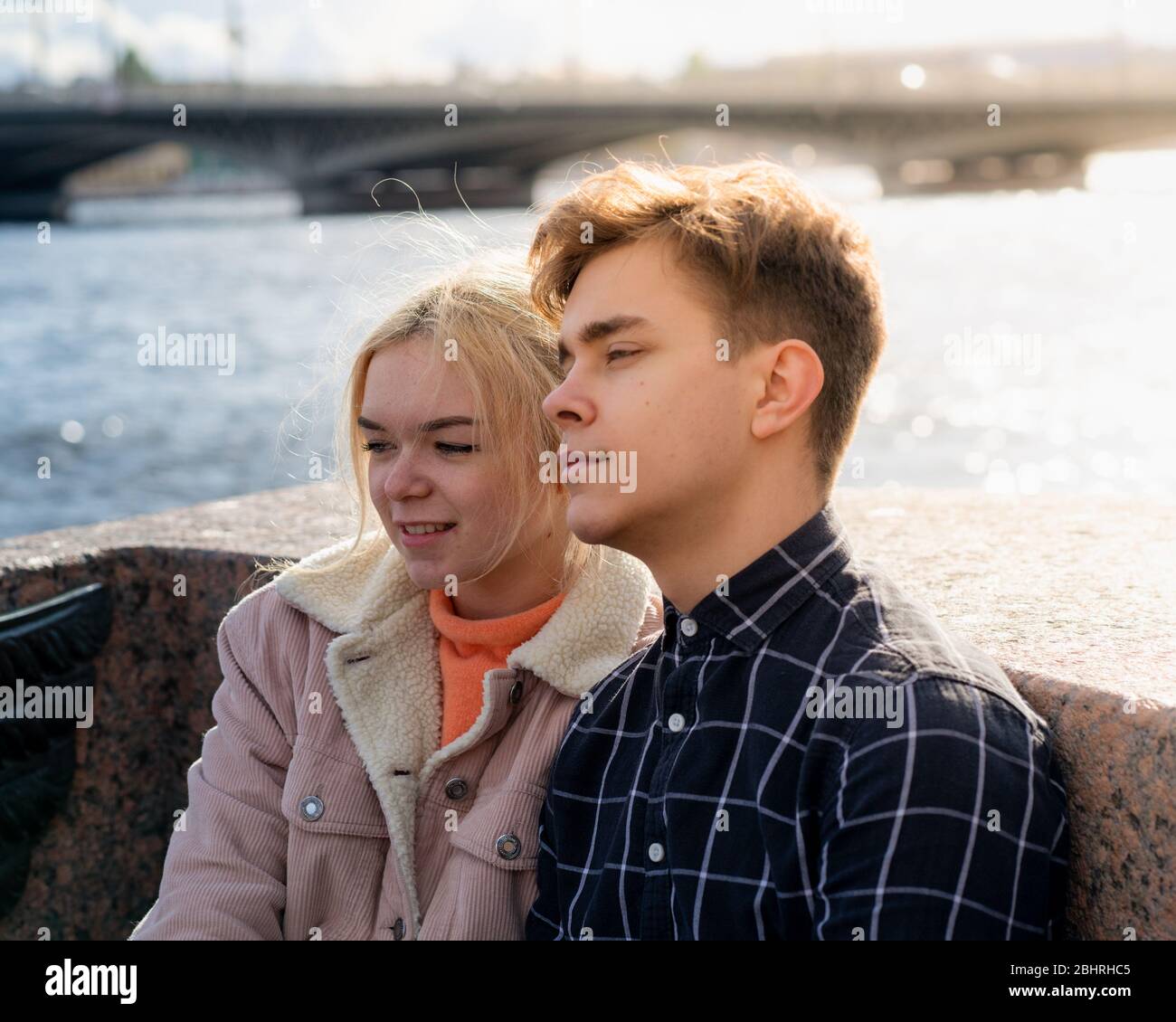Teenagers in love sit on the waterfront in the city center, resting in ...