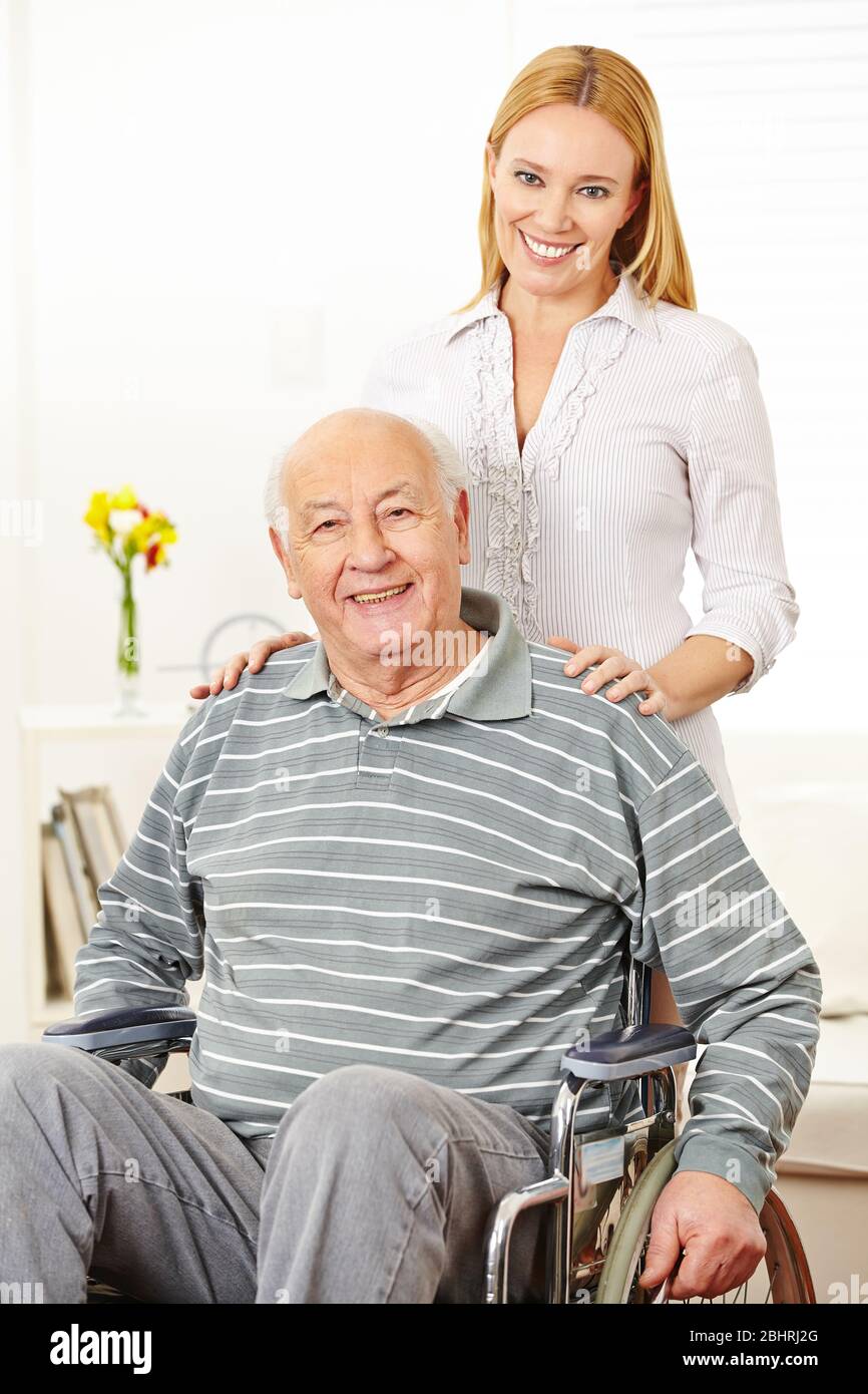 Smiling senior with disabilities in a wheelchair is cared for by his ...