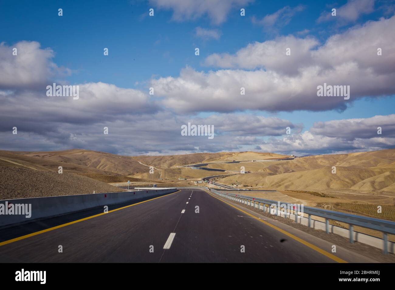 Asphalt road and bright blue sky with fluffy clouds . Empty desert ...