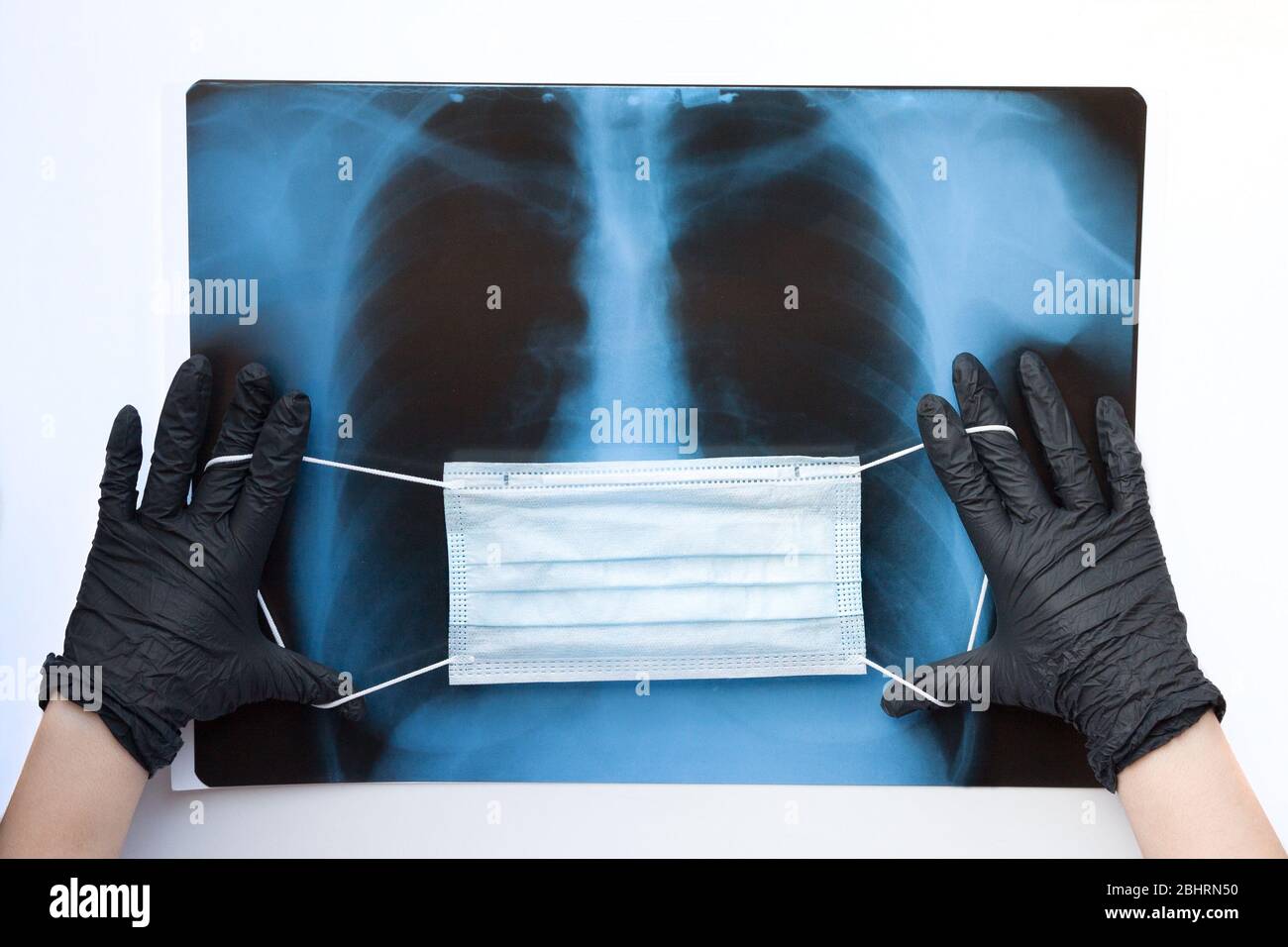 Blue respiratory mask on x-ray of human lungs in hands in black gloves ...