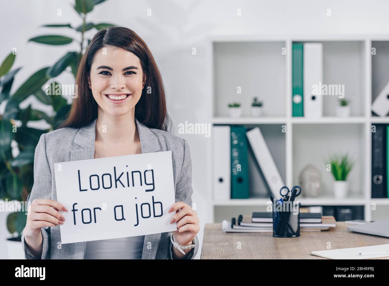 Employee smiling and showing placard with looking for a job lettering ...