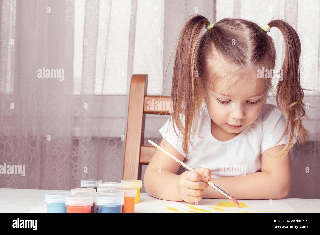 a girl with pigtails sits by the window during the day and paints the ...