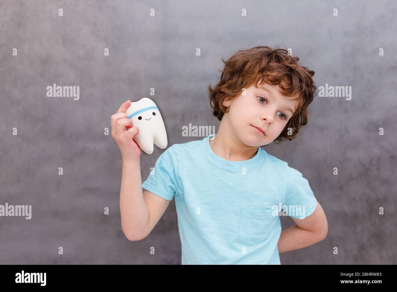 cute curly boy holds big tooth. The concept of children's health ...