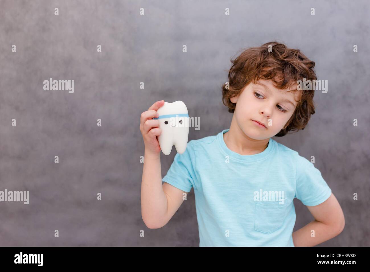 cute curly boy holds big tooth. The concept of children's health ...