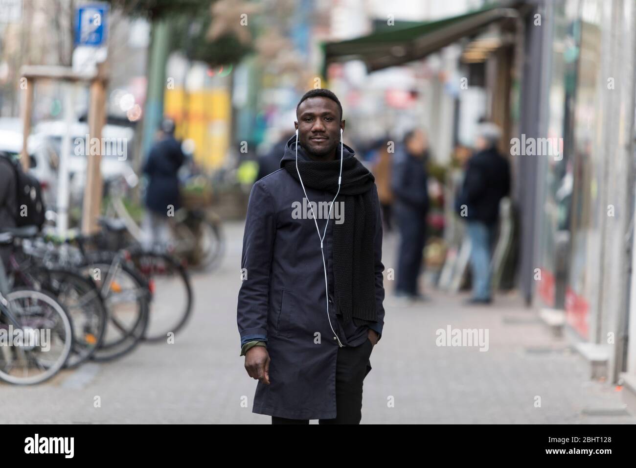 Handsome black man with earphones and coat posing on sidewalk Stock ...