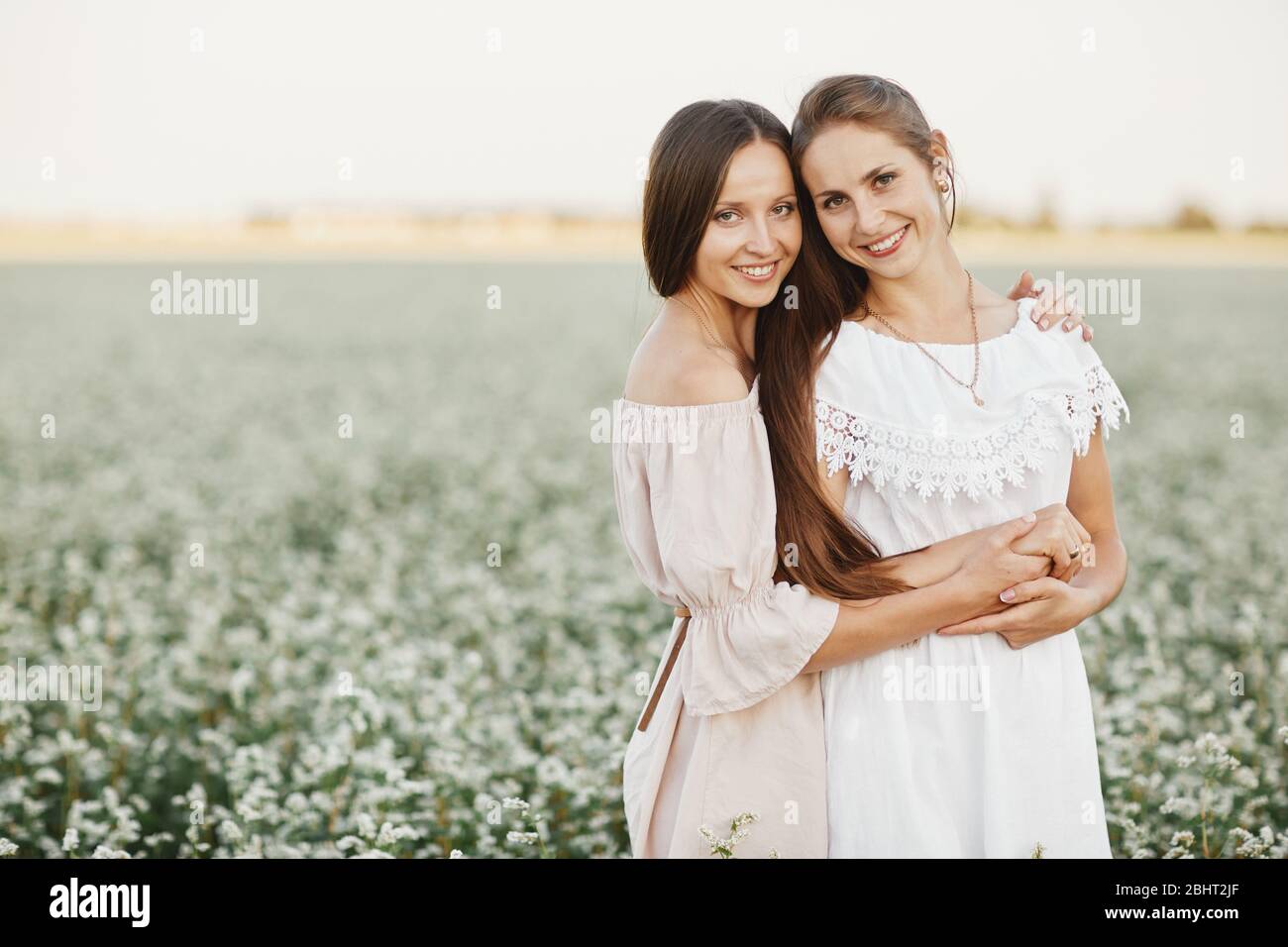 Two beautiful girls with long hair in a blooming field at sunset. two ...