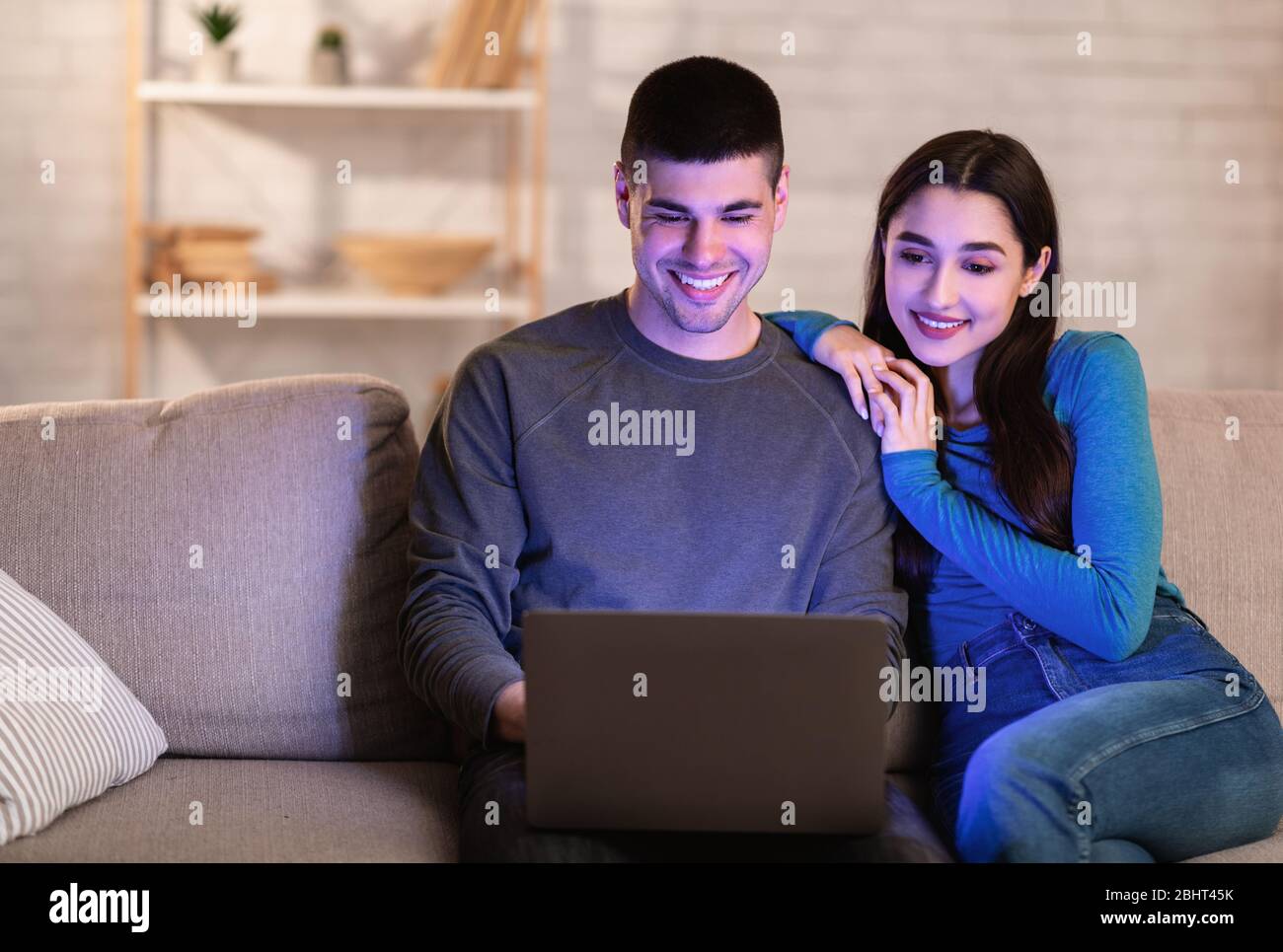 Happy couple using pc sitting on cozy couch Stock Photo - Alamy