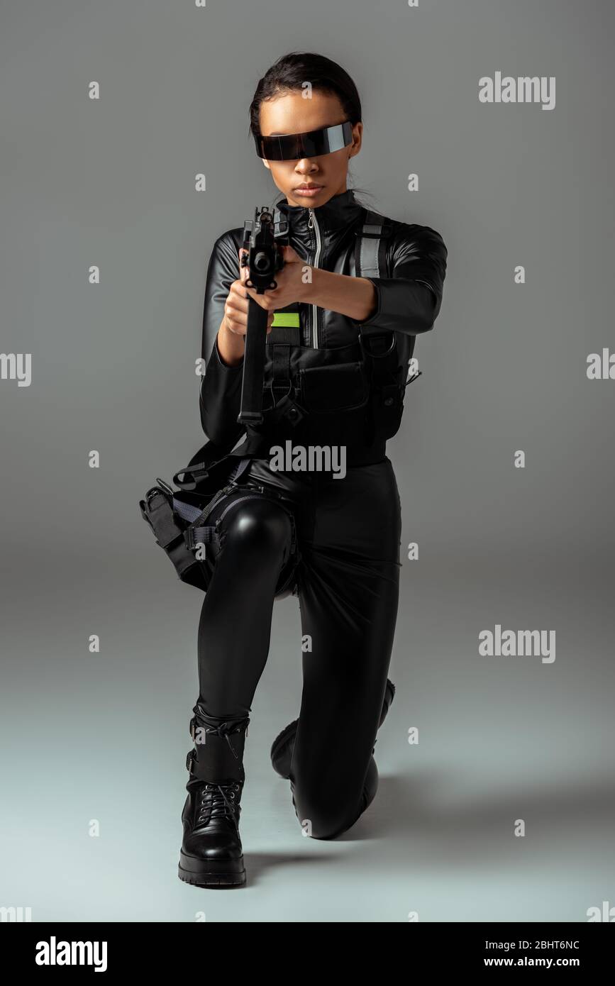 futuristic african american woman in glasses aiming assault rifle while ...