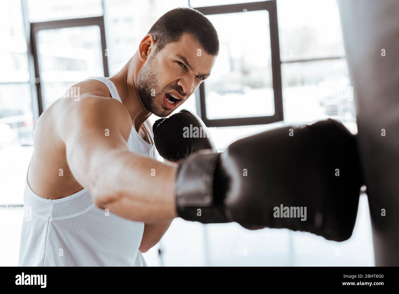 selective focus of angry sportsman in boxing gloves exercising with ...