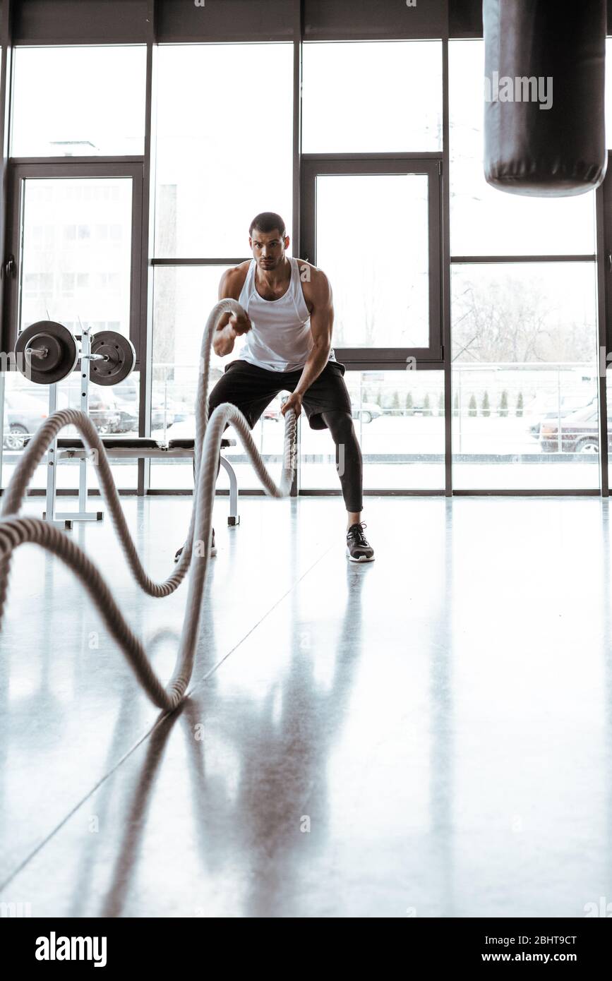 selective focus of handsome sportsman exercising with battle ropes in ...