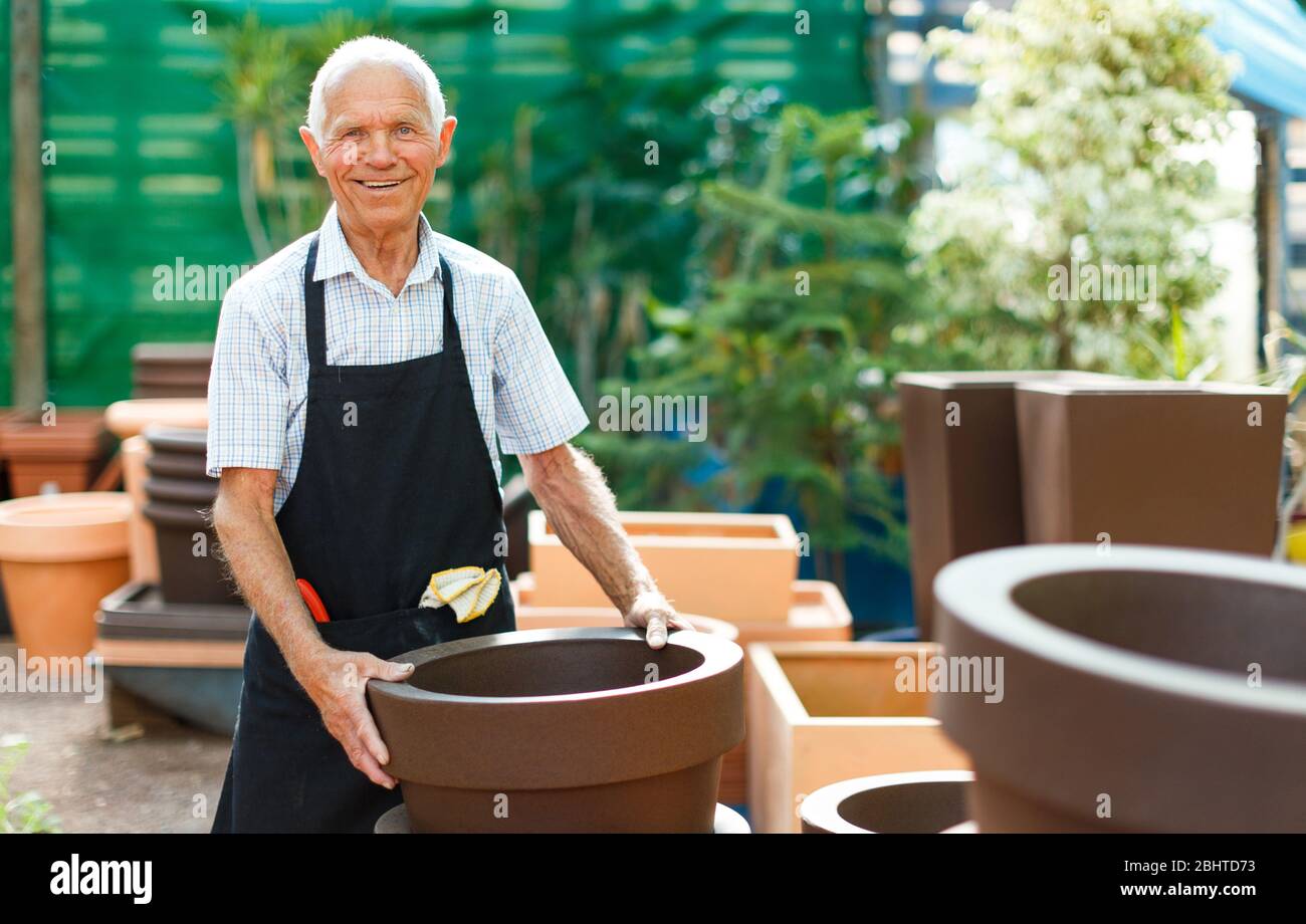 Senior owner of greenhouse choosing pots for plants in garden material ...