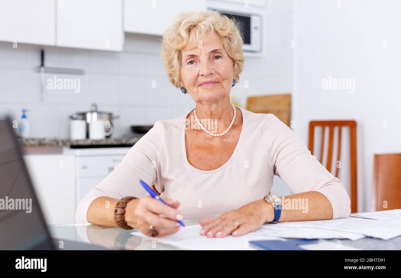 Senior woman sitting and filling up documents at kitchen table Stock ...