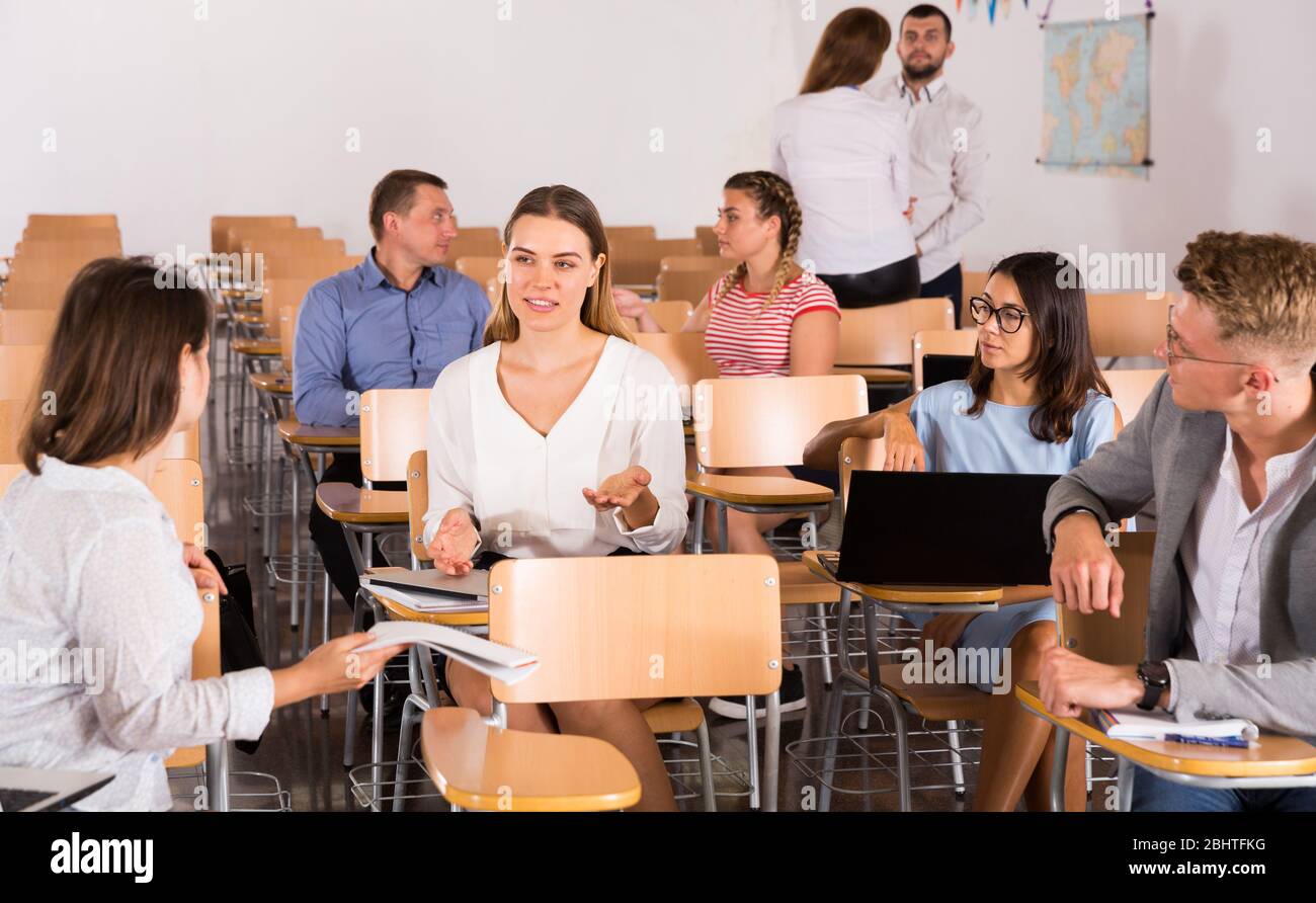 Happy group of adult students lively chatting while enjoying free time ...