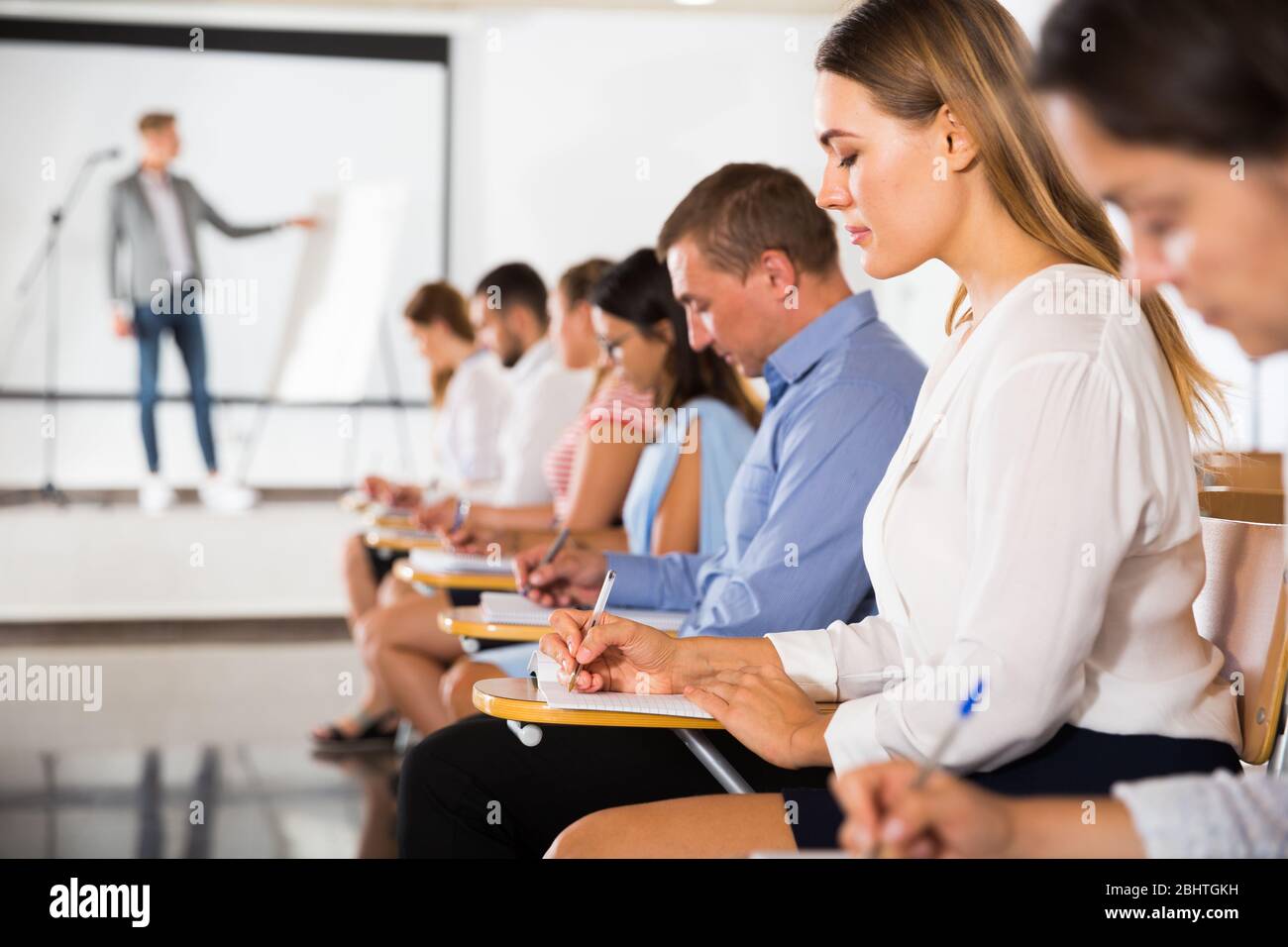 Side view of row of people listening lecturer and making notes at ...