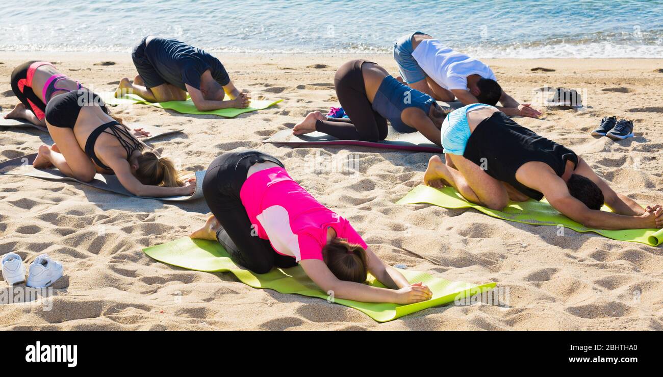 Yoga on beach, group of people practicing healthy lifestyle Stock Photo ...