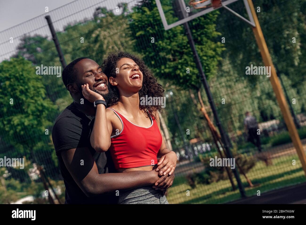 Outdoors Activity. African couple standing on basketball court hugging ...