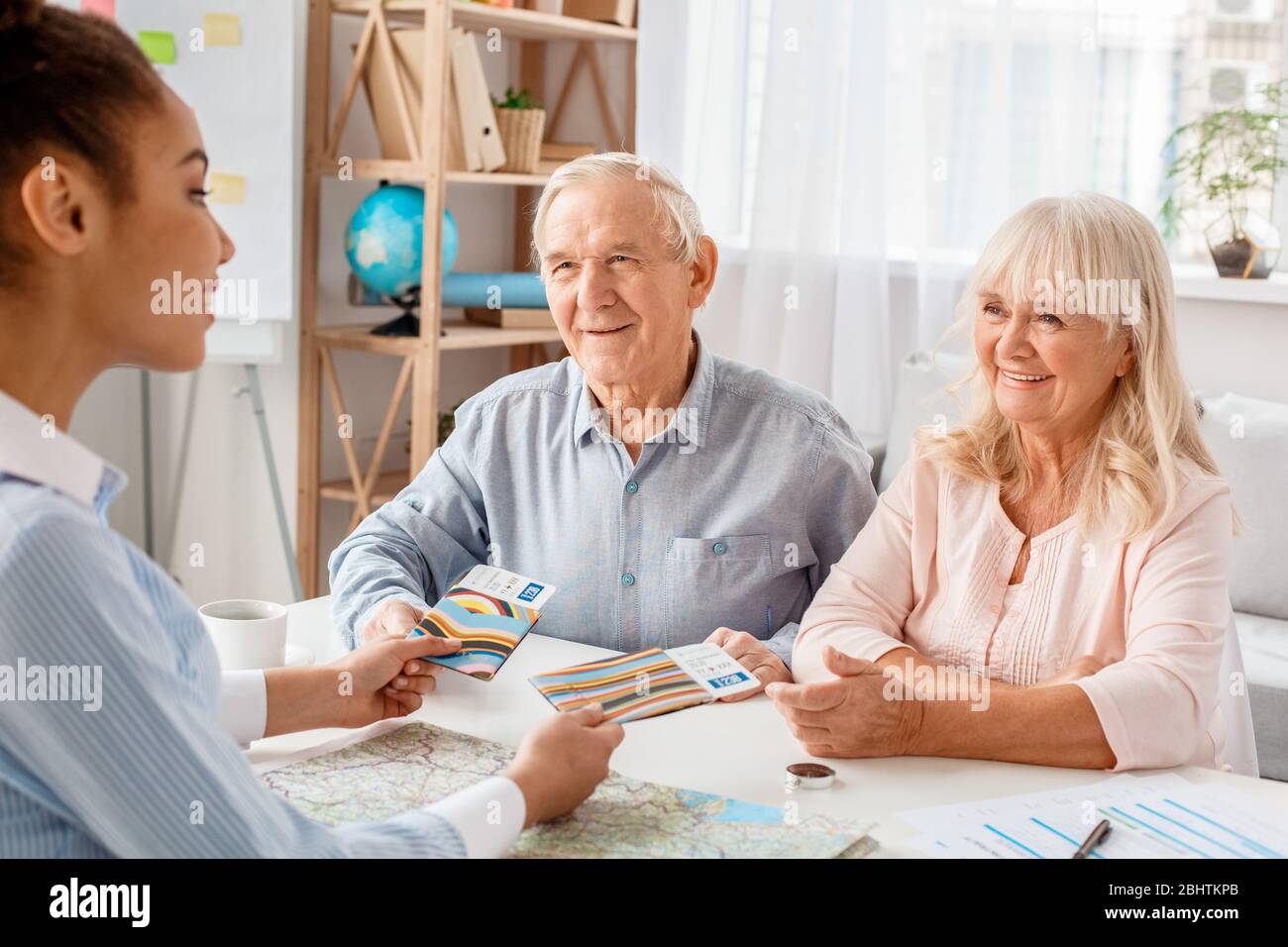 Travel agent at office sitting giving tickets and passports to senior ...