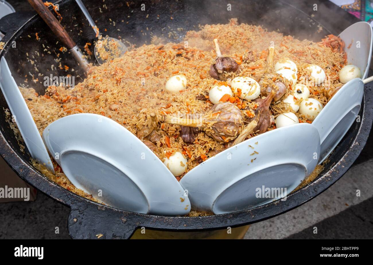 Cooking appetizing traditional oriental pilaf in a large cauldron ...