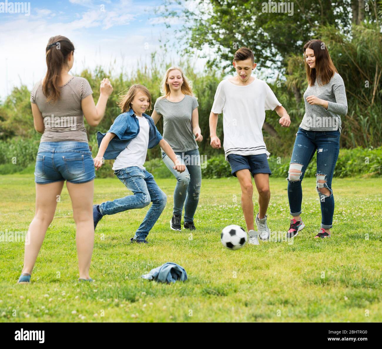 Three girls and two boys teenagers running with ball on meadow outdoors ...
