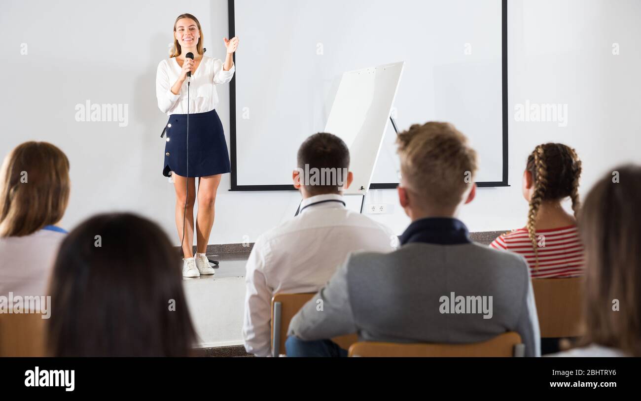 Smiling female coach giving presentation for adult audience in lecture ...